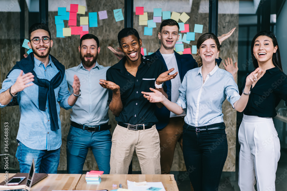 Portrait of positive team of young people in formal wear laughing at ...