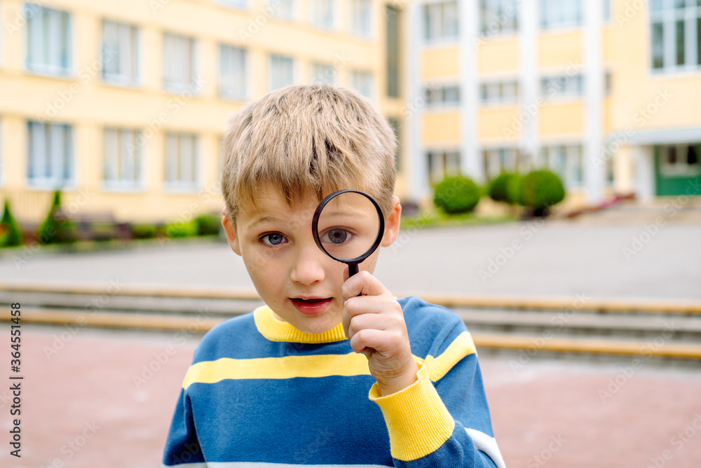 Curious surprised boy. One schoolboy with a magnifier near his eye in ...