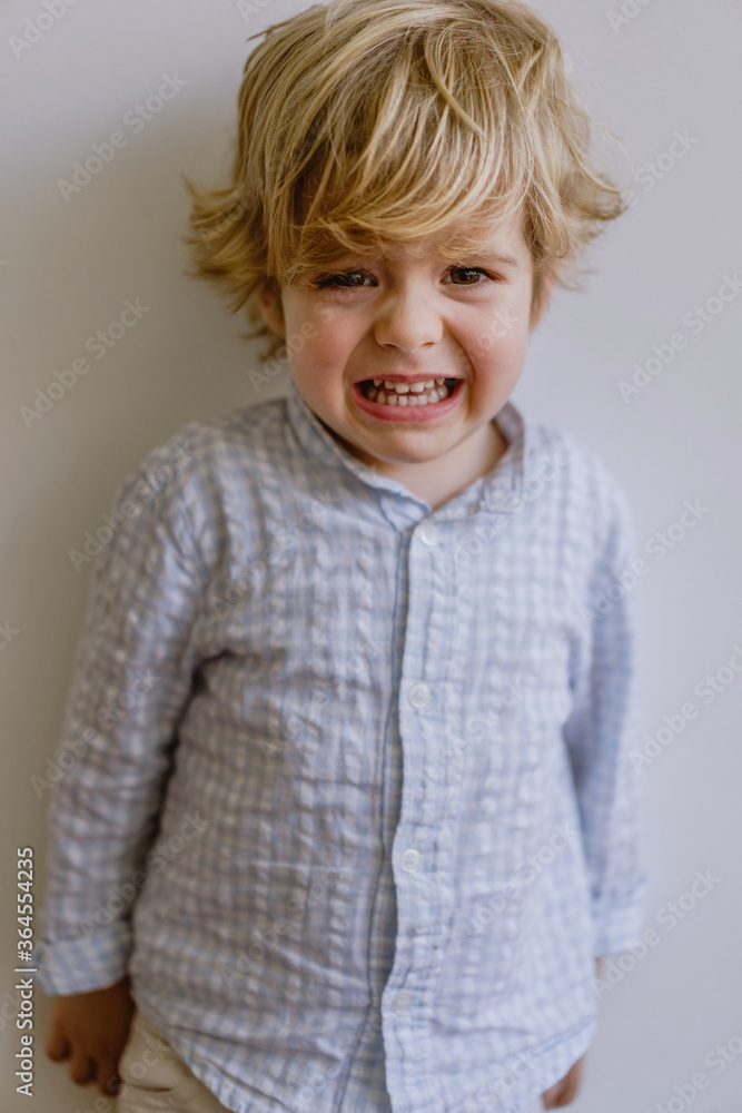 Disappointed little child in casual shirt standing near white wall and ...