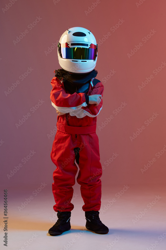 Cool boy child racer in helmet, racing suit, standing in neon light ...