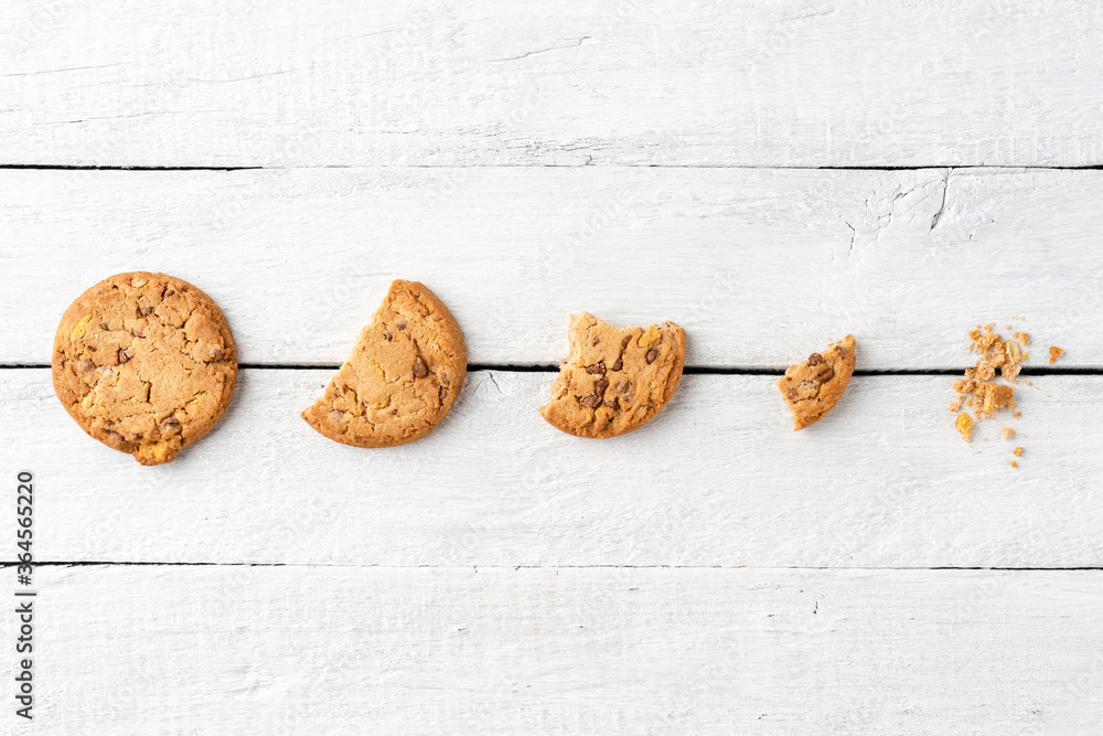 Five steps of chocolate chip cookies being devoured on white wooden ...