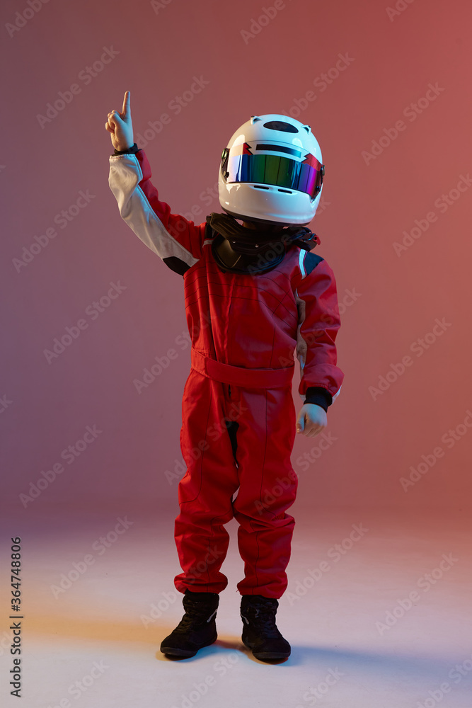 Boy child racer in helmet with raised hand, standing in neon light ...
