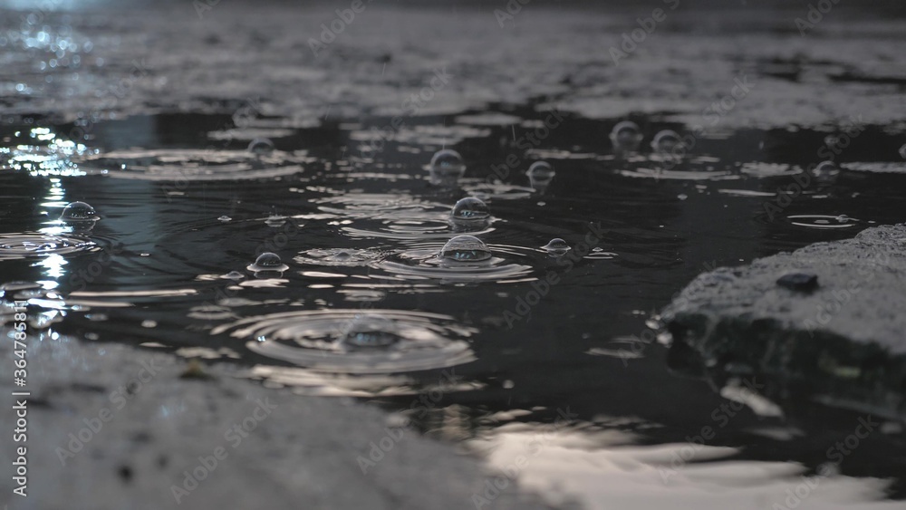 Drops of rain water fall into large puddle on the pavement, flooding ...