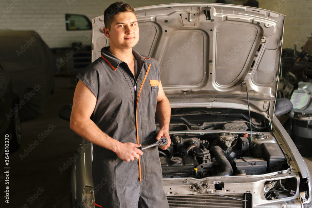 Mechanic looking straight ahead with a ratchet wrench with the hood of ...