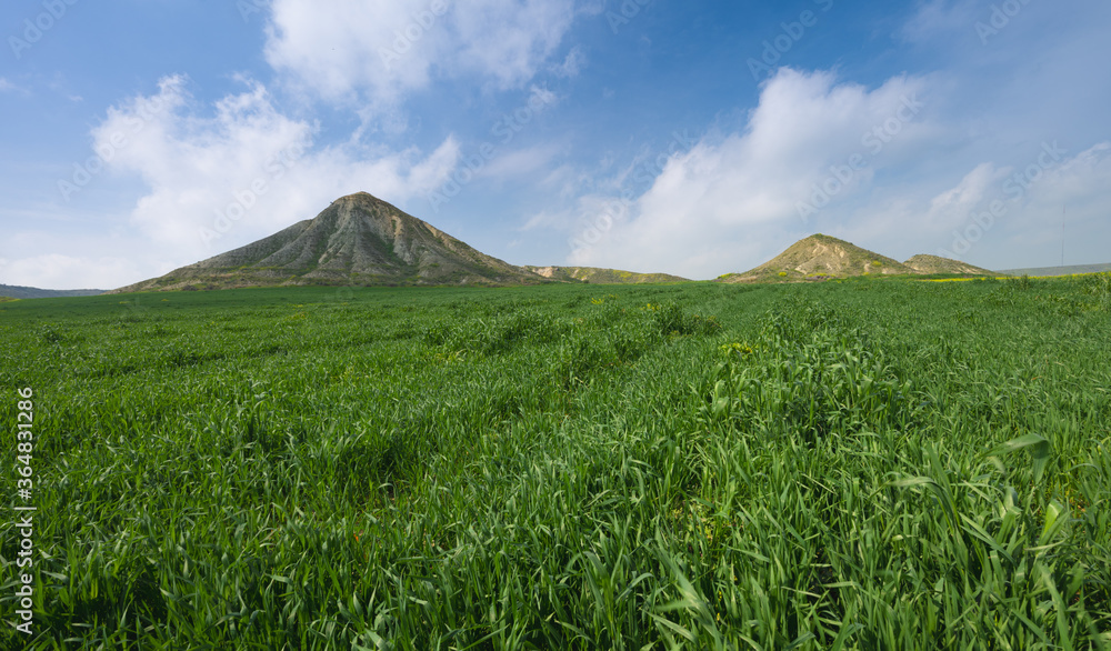 Breathtaking view of a single hill rising in a green field and a blue ...