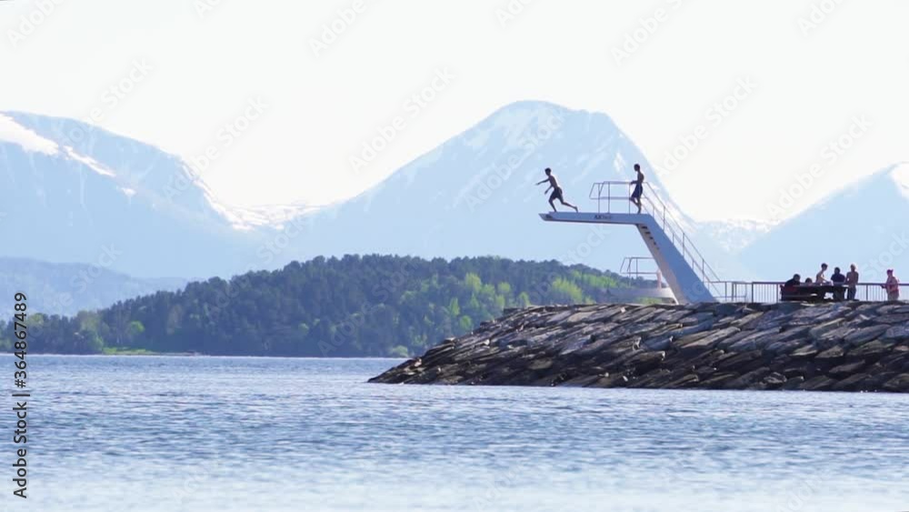 Slow motion shot of a person jumping off of a diving board into the sea ...