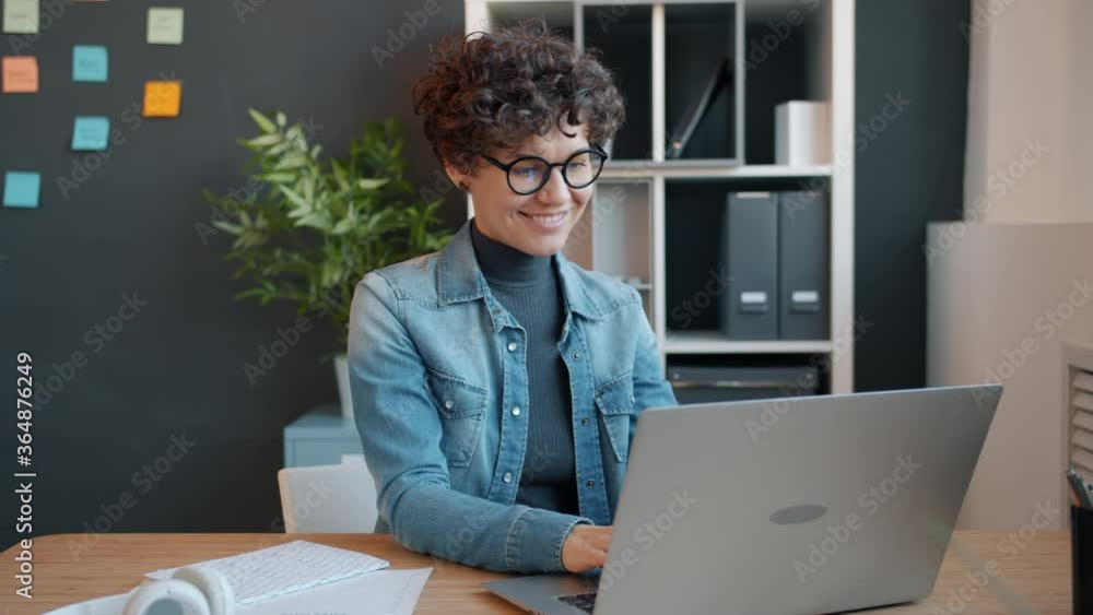Cheerful girl busy with laptop work in office typing and looking at ...