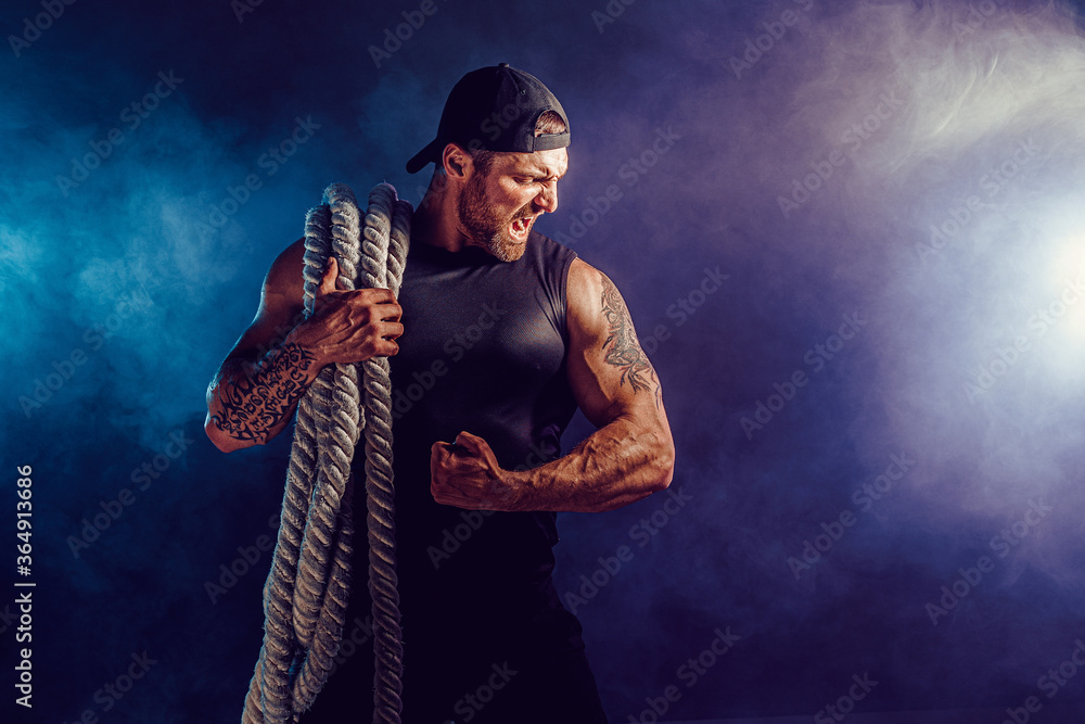 Bearded athletic looking bodybulder holding battle rope on dark studio ...