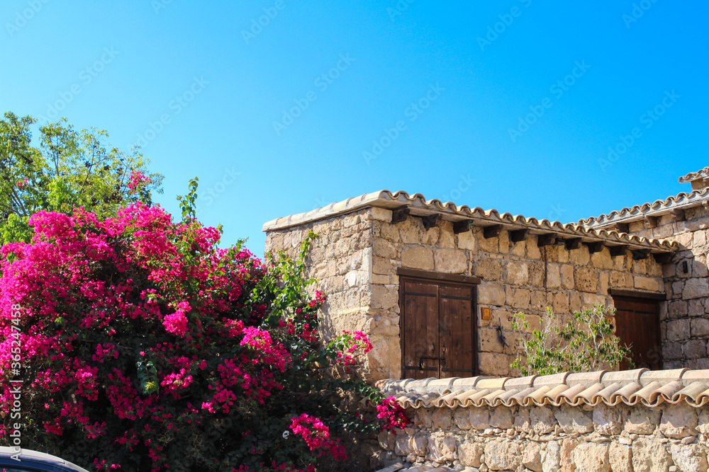 An old stone room with a tiled roof and wooden doors, next to a Bush in ...
