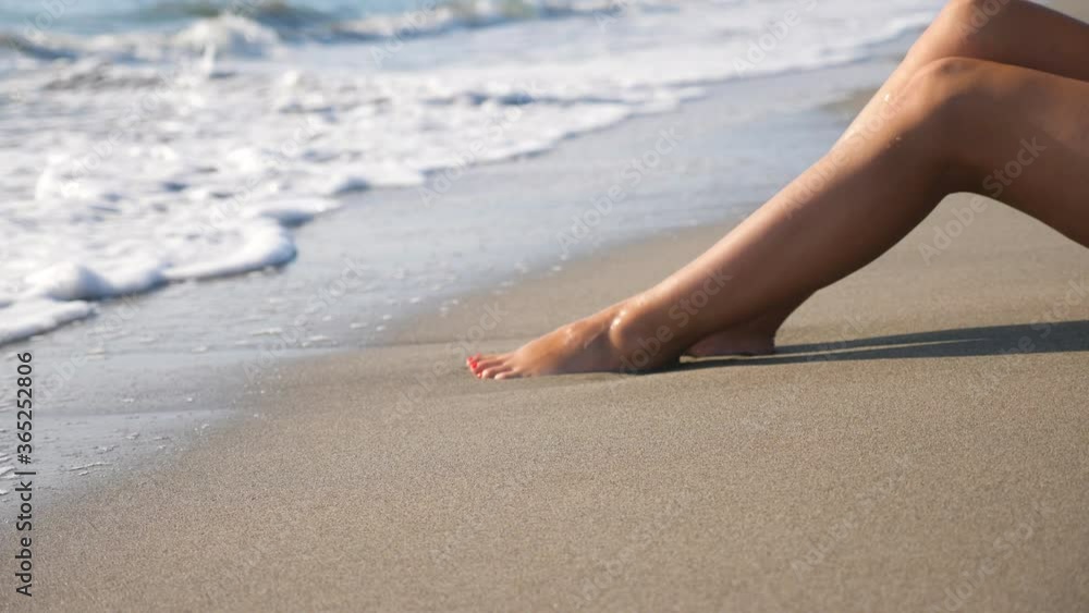 Slim legs of woman lying on tropical beach with splashing waves. Ocean ...