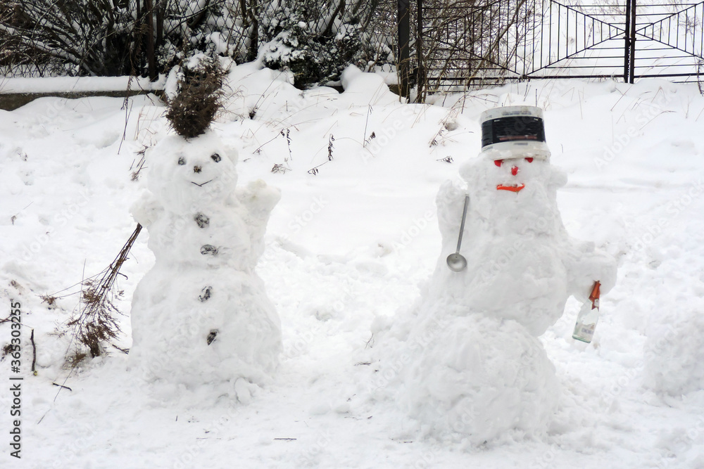 Two snowmen made of three snowballs, a wife snowman holding a broom ...