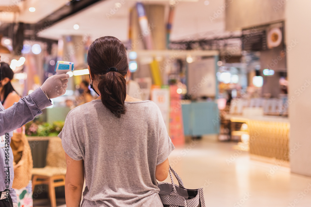 Security guard checking woman temperature at shopping mall entrance ...