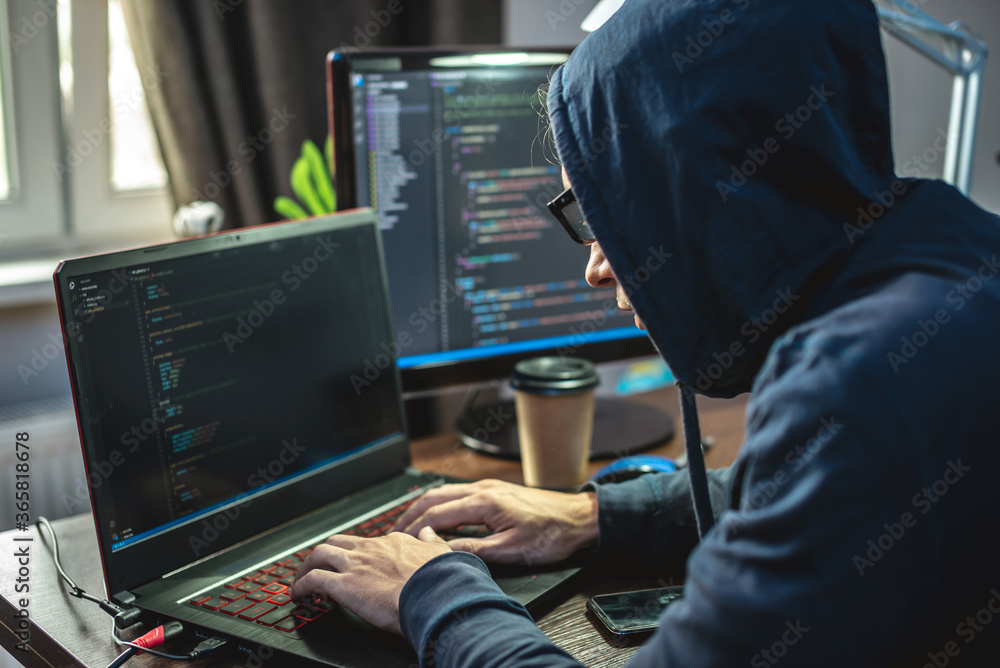 Hacker in the hood is programming virus code at the keyboard for the ...