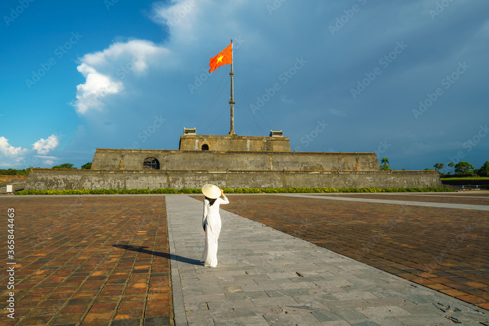 Ky Dai flag tower at Ngo Mon square with Vietnamese girl wearing traditional dress Ao Dai in the ...