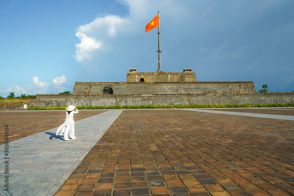Ky Dai flag tower at Ngo Mon square with Vietnamese girl wearing traditional dress Ao Dai in the ...