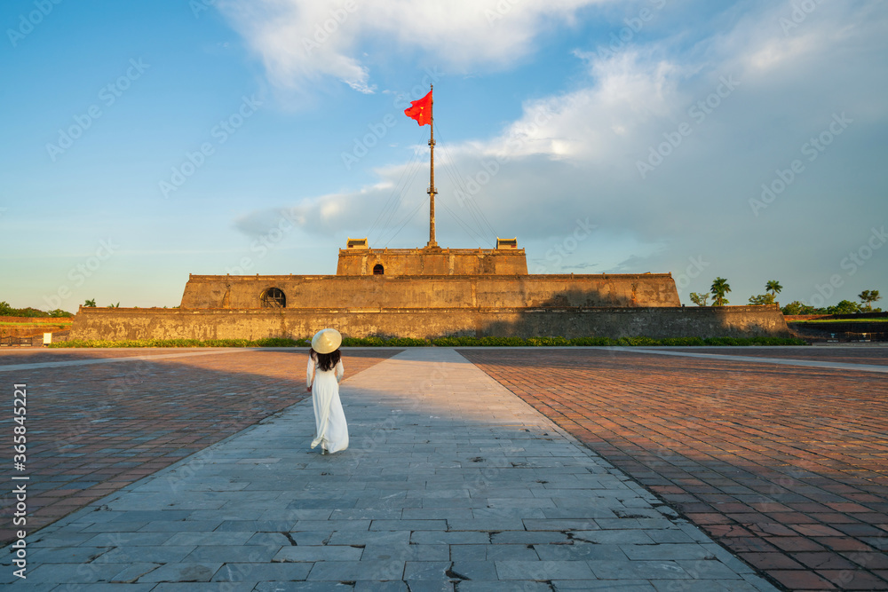 Ky Dai flag tower at Ngo Mon square with Vietnamese girl wearing traditional dress Ao Dai in the ...
