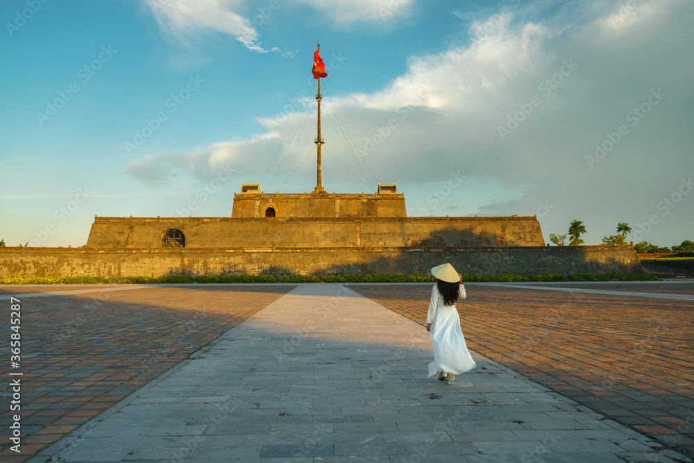 Ky Dai flag tower at Ngo Mon square with Vietnamese girl wearing traditional dress Ao Dai in the ...