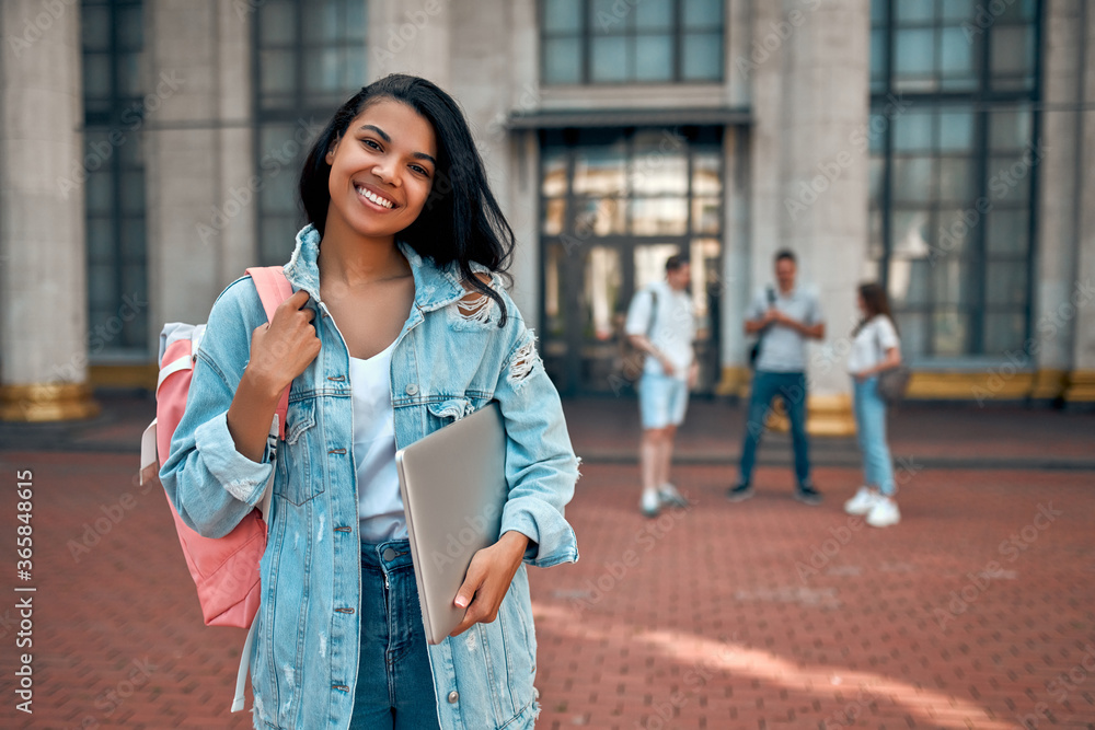 Cute African American girl student with a backpack and laptop near the ...