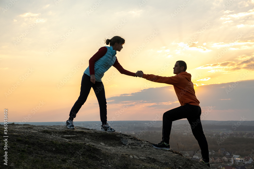 Man and woman hikers helping each other to climb stone at sunset in ...