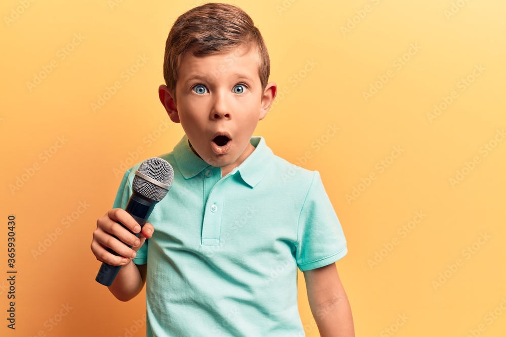 Cute blond kid singing song using microphone scared and amazed with ...