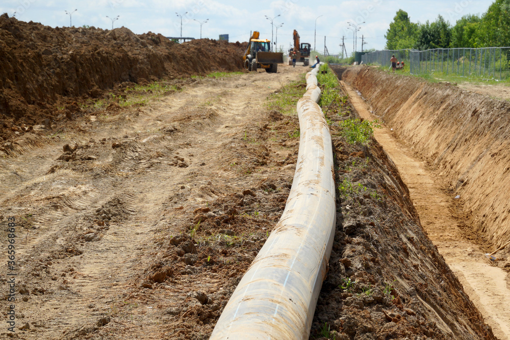 A long plastic pipe lies next to the trench ready to be laid in it ...