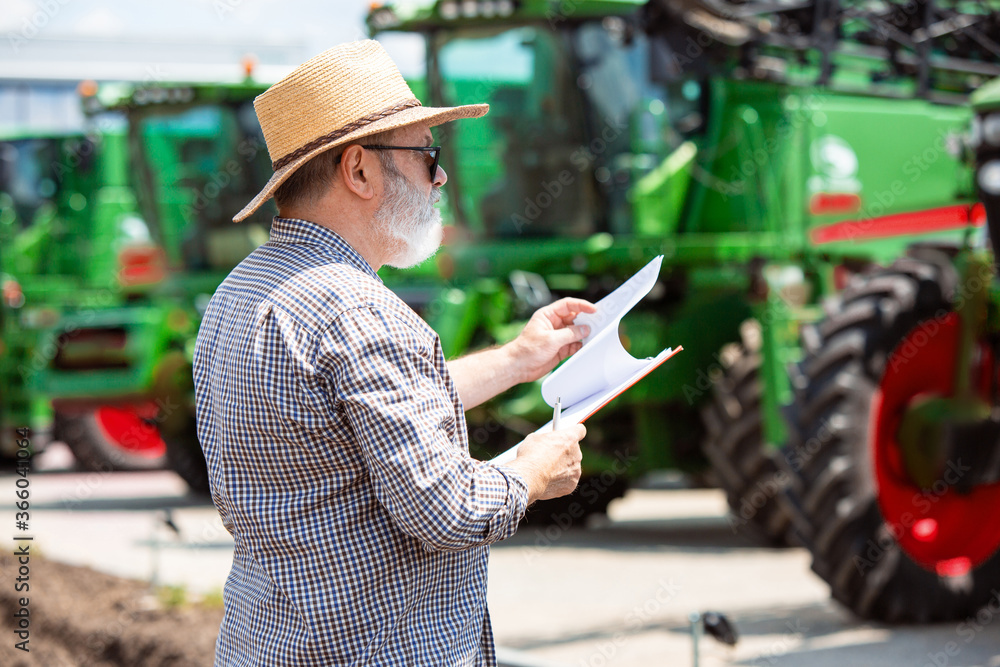 Professional farmer with a modern tractor at work with documents. Looks ...