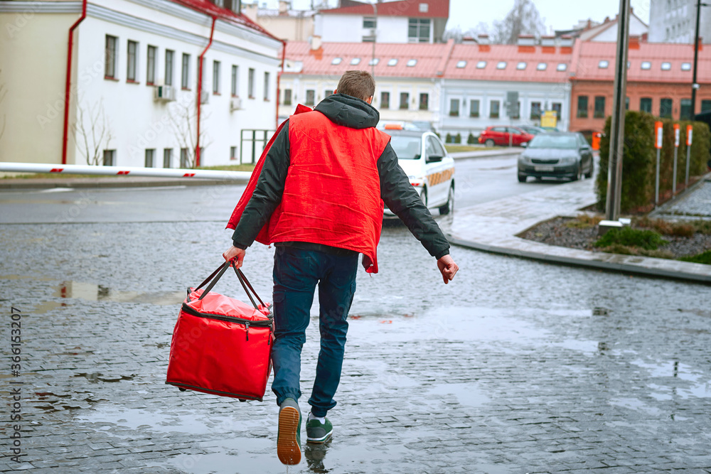 Delivery boy delivering food to costumers, walking with red thermal bag ...