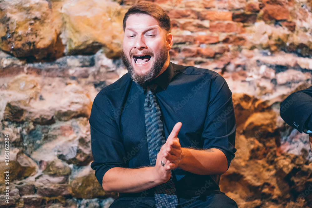 Bearded singer clapping hands while singing against wall in club Stock ...