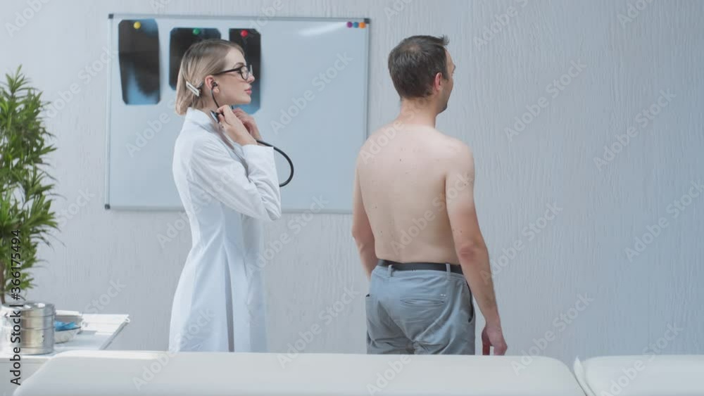 A friendly young doctor in a white coat examines a male patient using a ...