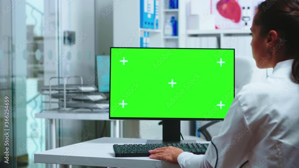 Doctor sits at computer with blank green screen display in hospital ...