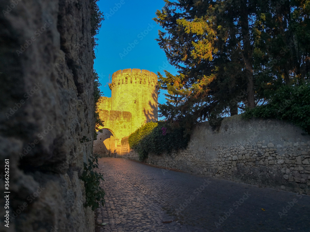 Cobbled street of a medieval village with arch in the walls and tower ...