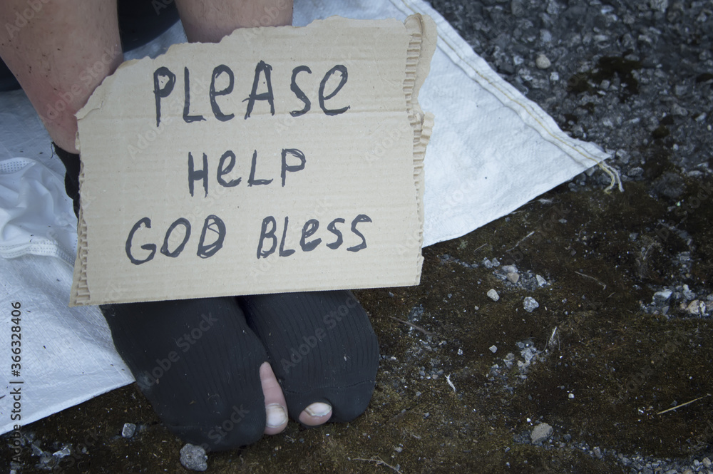 Feet of a homeless man sitting on the street in torn socks and a sign ...