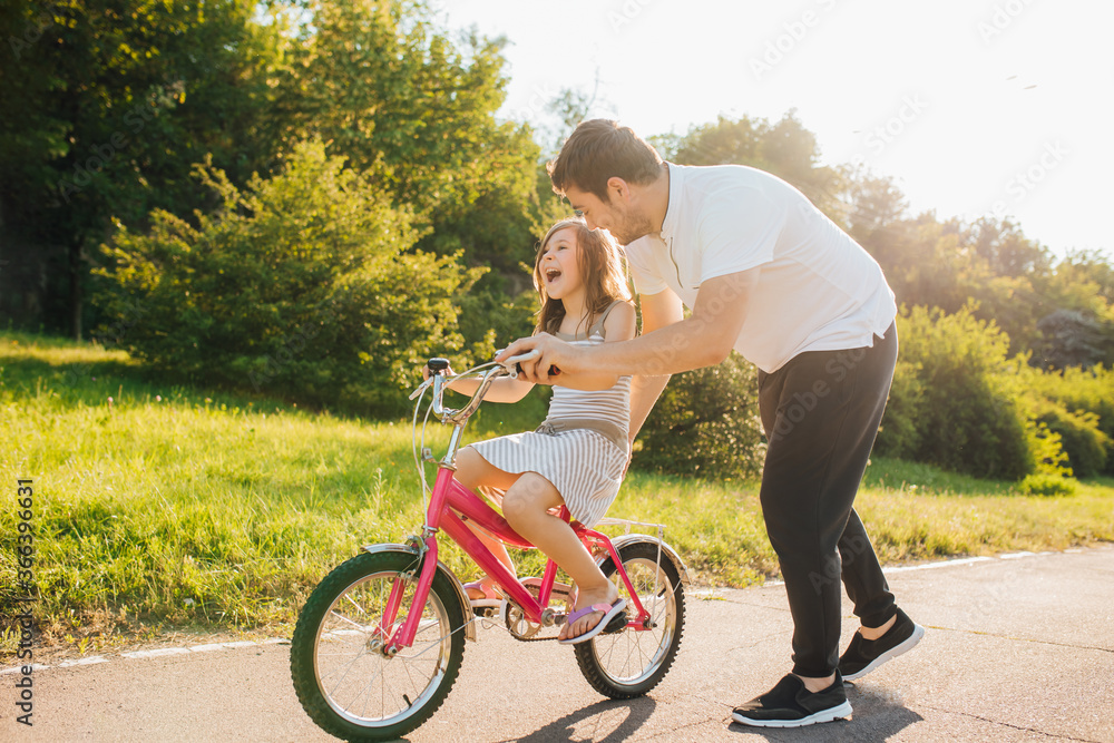 Little girl learning ride bicycle with father. Young father teaching his daughter to ride ...