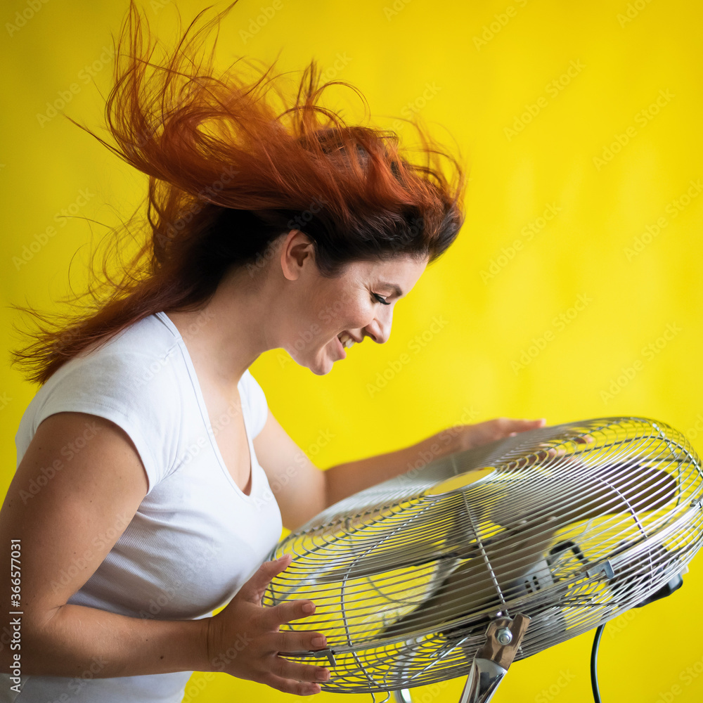 A beautiful red-haired woman is cooled off standing over a large ...