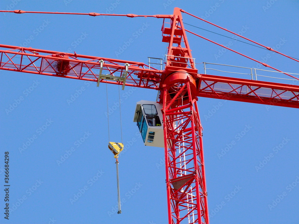 Red tower crane detail with yellow hoist under blue sky. vertical truss ...