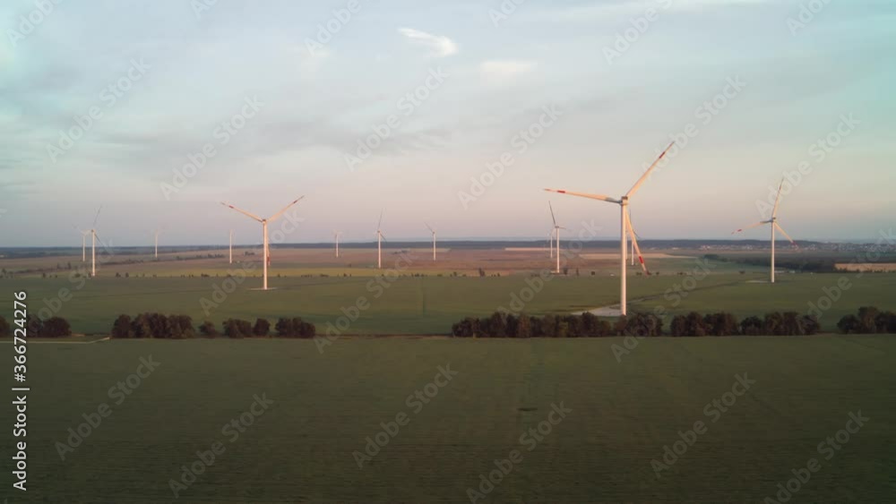 Wind power plant in the green fields at sunset. Camera flying parallel ...