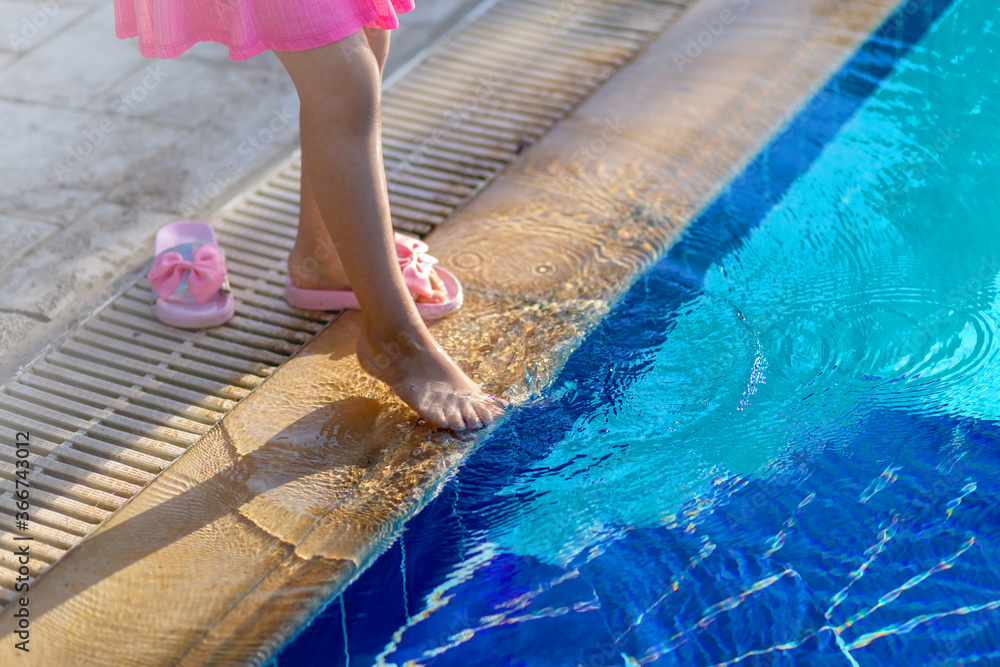 Young child girl in pink dress and shoes standing barefoot at the edge ...