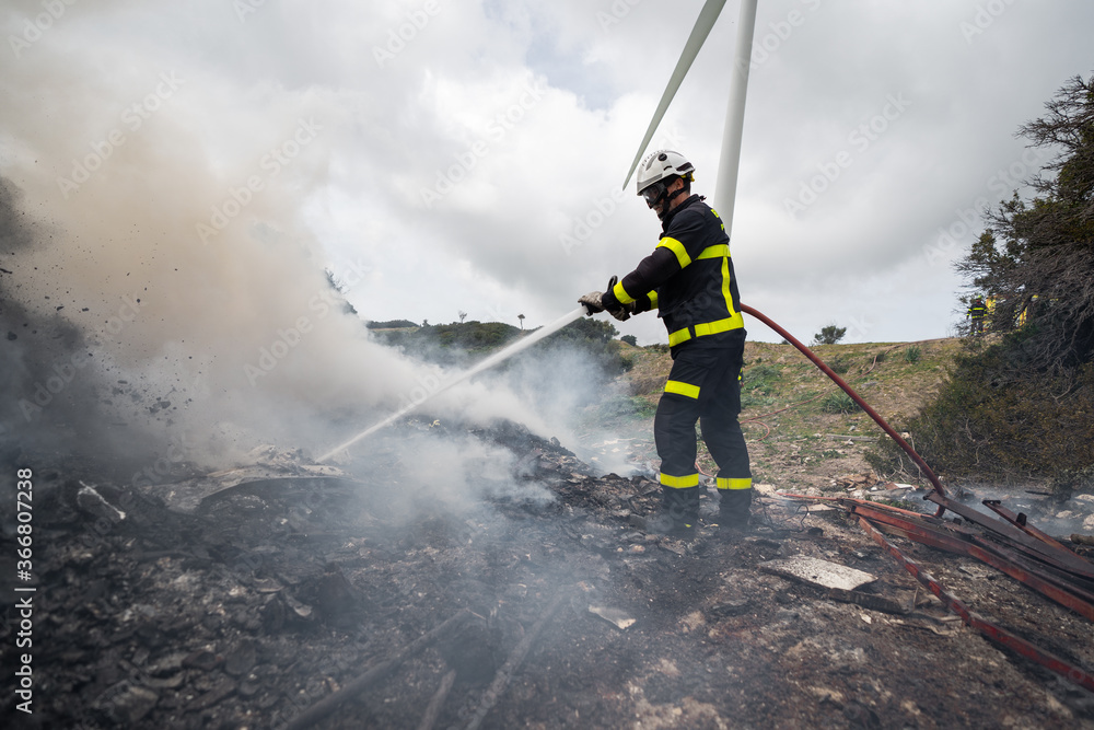 Side view of brave fireman in protective uniform standing with hose and ...
