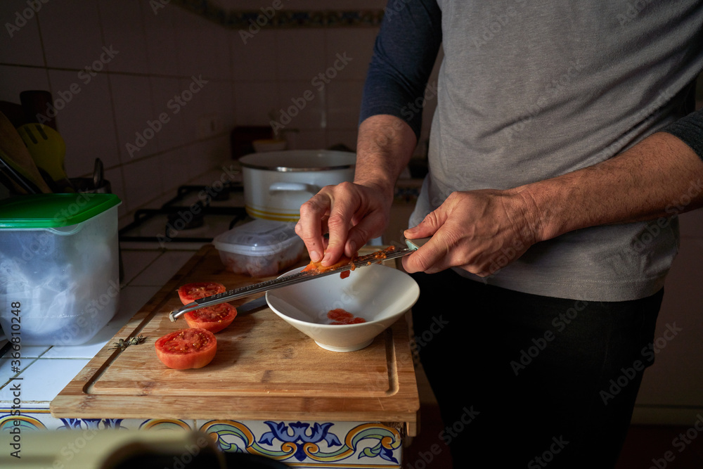 Stock photo of a man grating tomato on top of a piece of wood in a ...