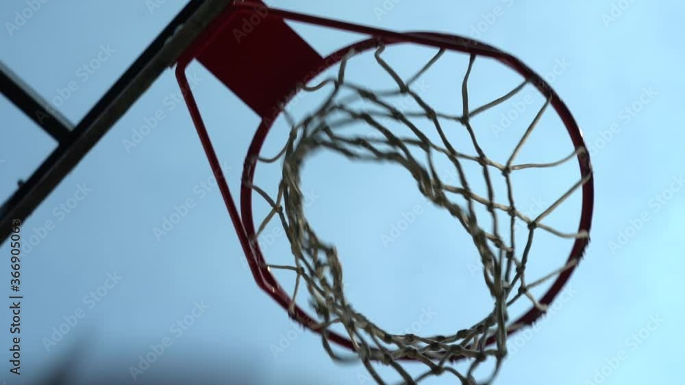 An old battered basketball ball falls through the hoop towards the ...