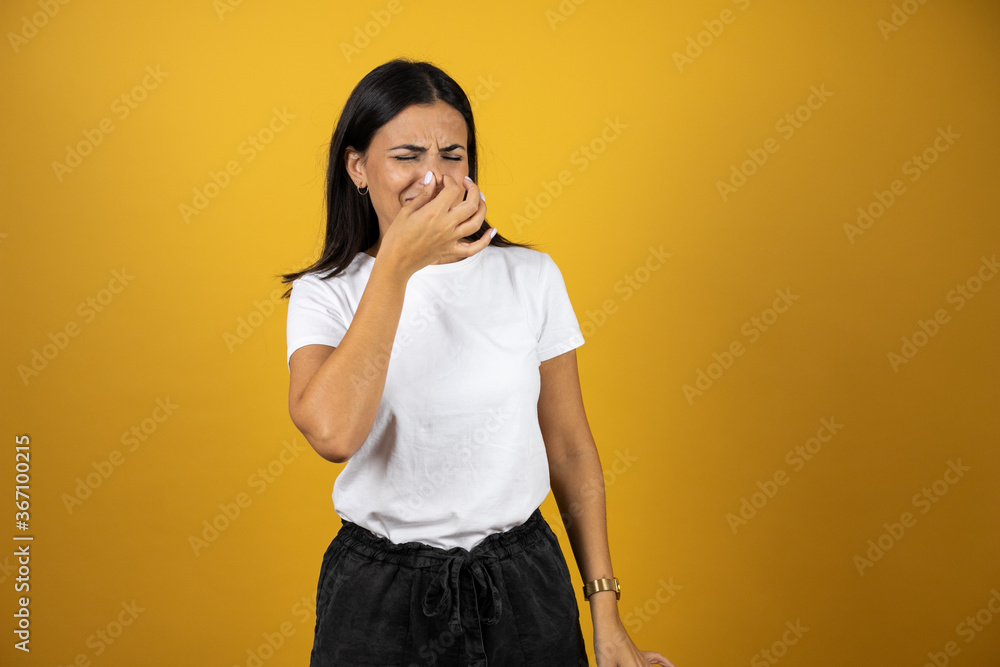 Young beautiful woman standing over isolated yellow background smelling ...