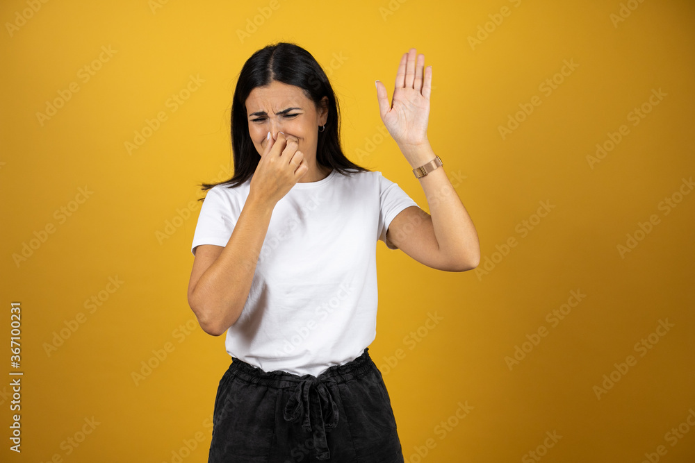 Young beautiful woman standing over isolated yellow background smelling ...
