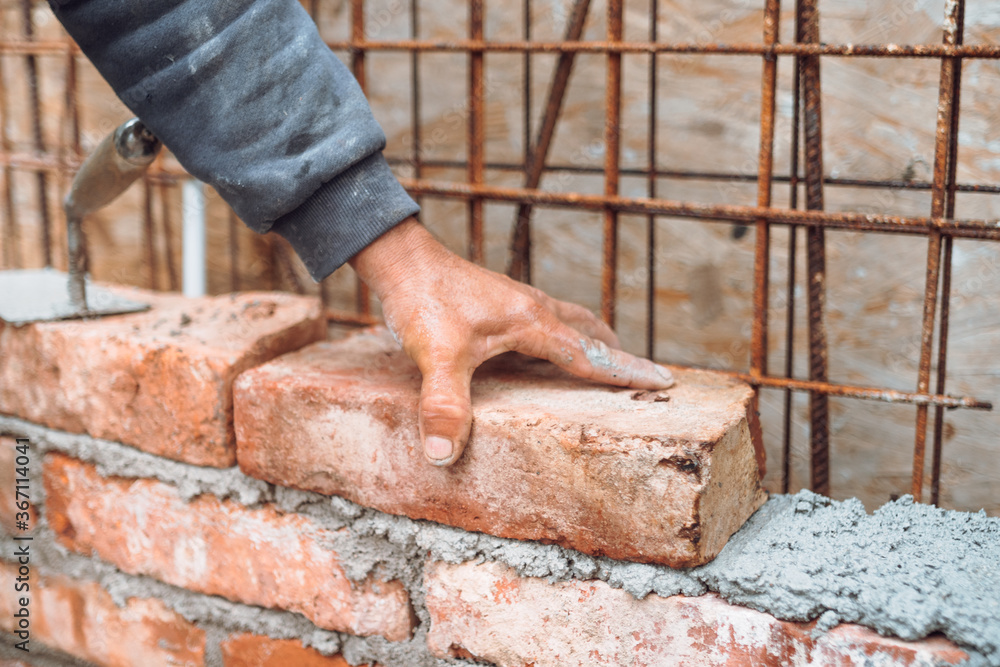 details of worker, bricklayer placing and adjusting bricks ...