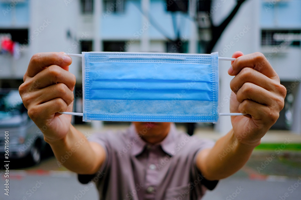 Man holding up surgical mask in neighbourhood. Now mandatory to wear ...