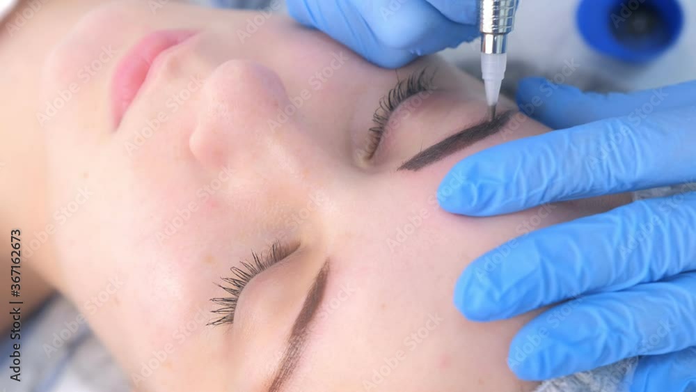 Cosmetologist making eyebrows microblading procedure in beauty salon ...