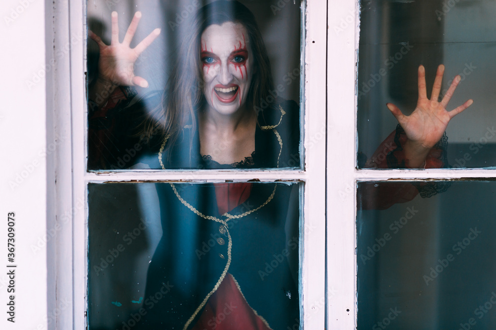 Beautiful witch poses behind window in front of the camera with bright ...