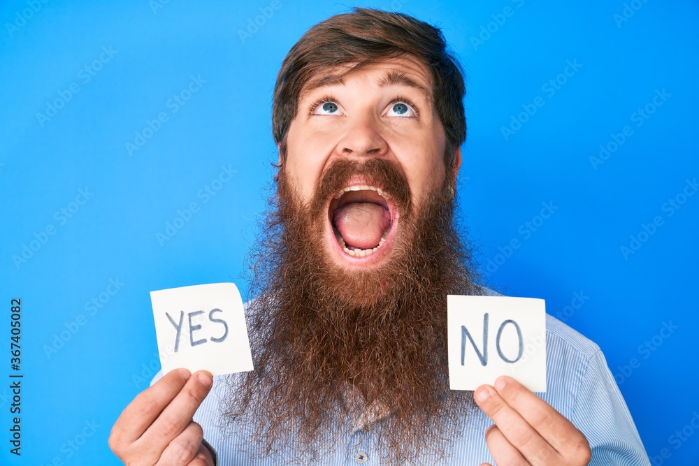 Handsome young red head man with long beard holding yes and no reminder ...