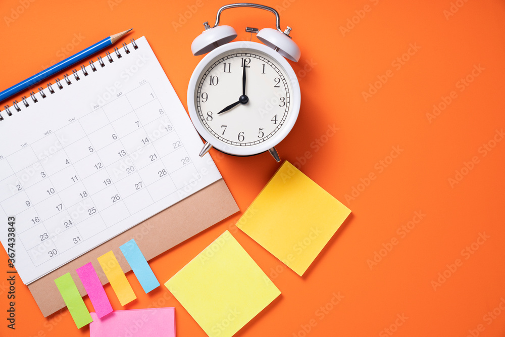 close up of alarm clock and calendar on the orange table background ...