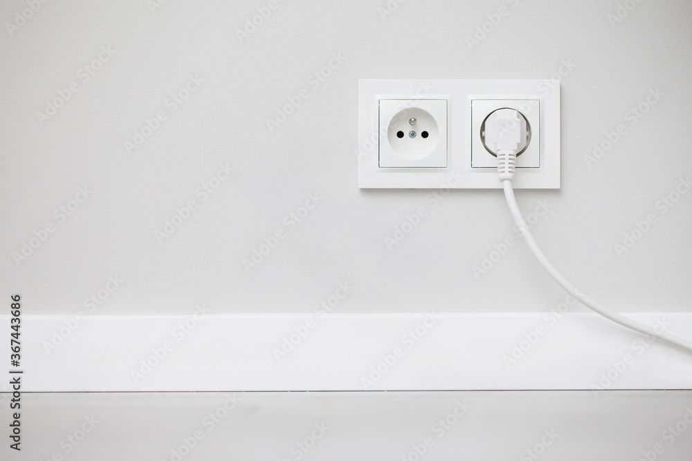 Electrical socket isolated on gray wall. White wire plug plugged in ...