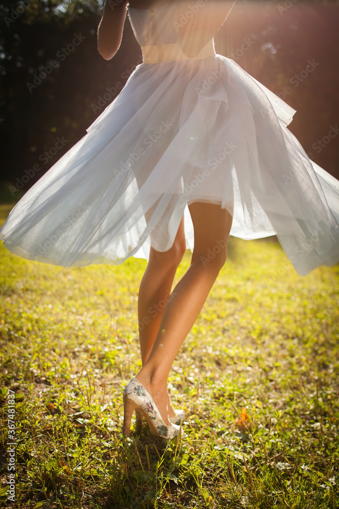 A young girl bride in a short wedding dress is spinning in the rays of ...